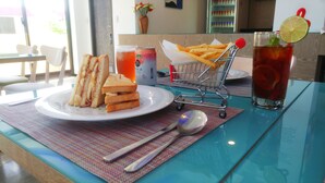 Uma mesa de jantar com um prato de sanduíches, uma lata de bebida, um copo de chá gelado, um carrinho de compras pequeno com batatas fritas e uma colher.