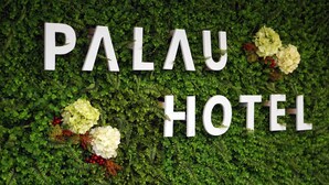 Nome de um hotel escrito em letras brancas grandes sobre um fundo de folhagem verde.