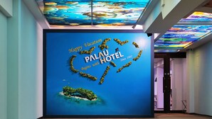 Interior de hotel com um grande mural na parede retratando uma ilha tropical e o texto "Happy Vacation Palau Hotel Desde 1982".