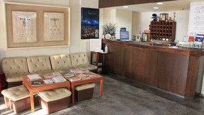 Uma área de recepção de hotel com um balcão de madeira, um sofá e uma mesa de centro com revistas.