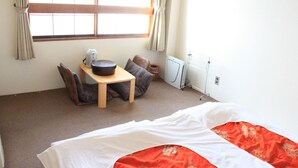 Quarto de hotel com uma cama, uma mesa pequena com uma chaleira, uma cadeira e uma janela com cortinas.