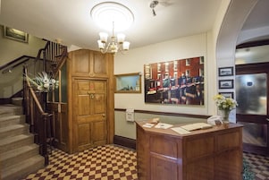 Uma área de recepção com um balcão de madeira, piso xadrez, escada e lustre.