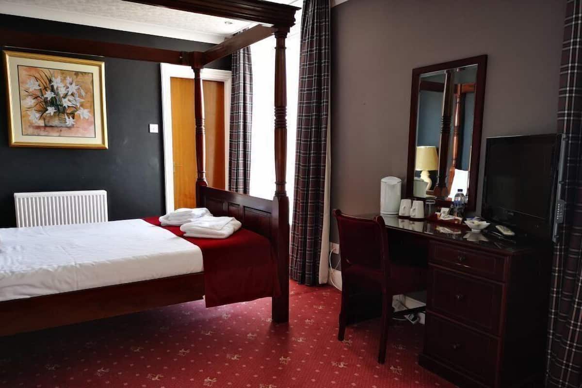 Quarto de hotel com cama de dossel, escrivaninha com espelho e televisão.