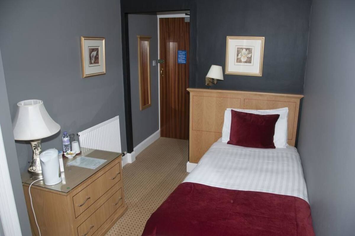 Quarto de hotel com cama, cômoda, luminária e quadros nas paredes.