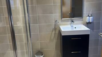 Uma casa de banho moderna com cabine de duche em vidro, lavatório com espelho e toucador com gavetas.