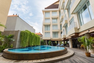 Pátio de hotel com piscina, área de estar ao ar livre e um edifício de vários andares com sacadas.