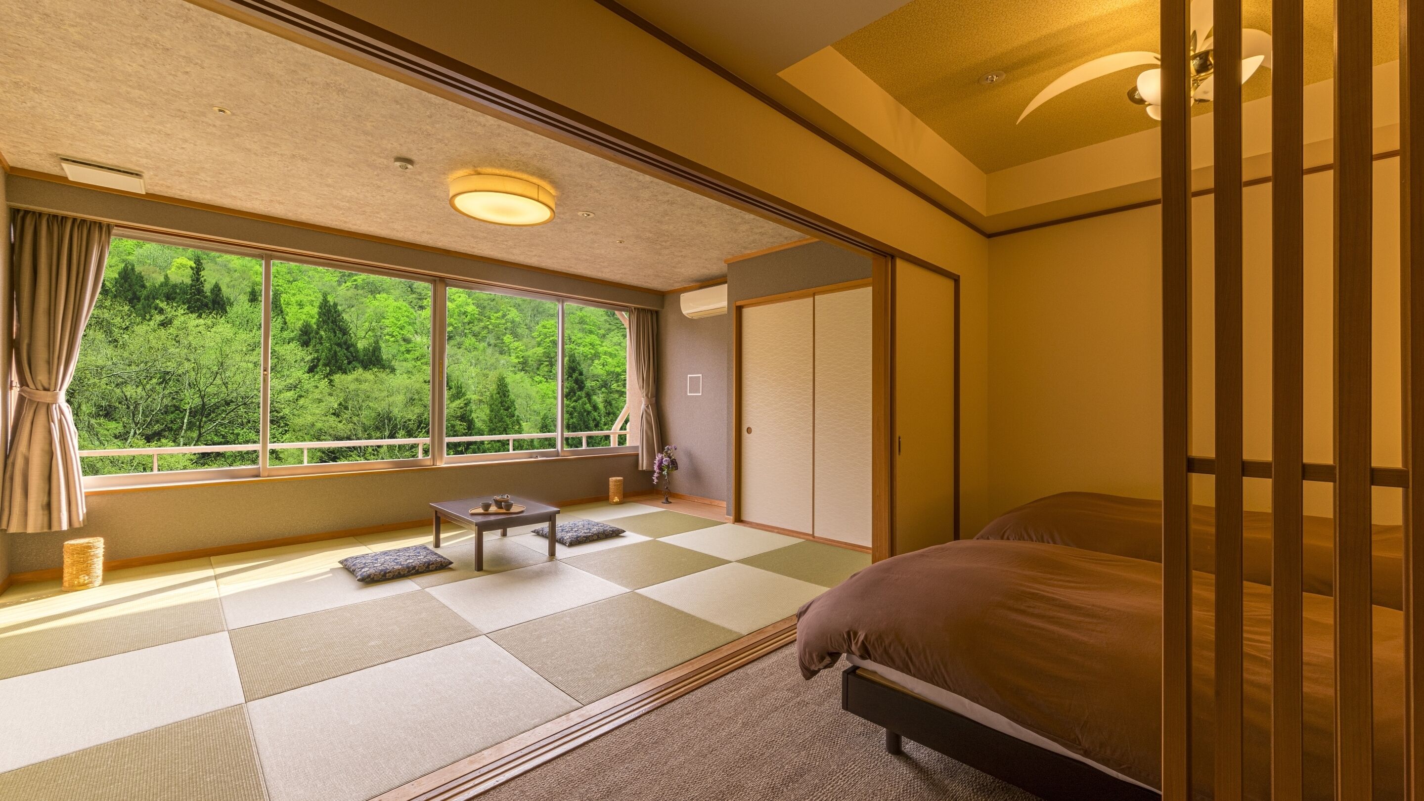 Um quarto tradicional japonês com piso de tatame, futon, uma pequena mesa com jogo de chá e vista para vegetação exuberante através de amplas janelas.