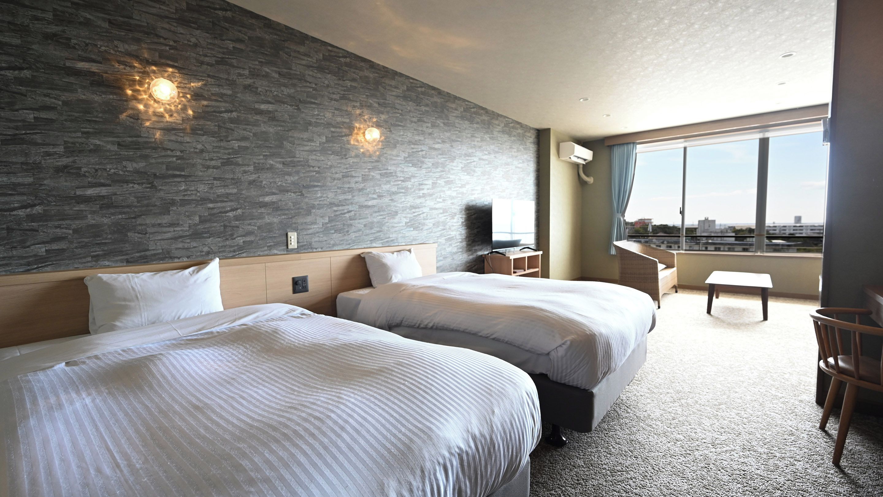 Quarto de hotel com duas camas, televisão, escrivaninha e vista para a cidade.