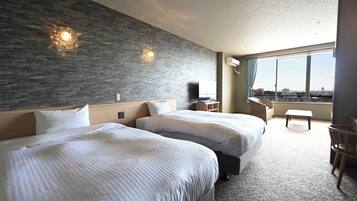 Quarto de hotel com duas camas, televisão, escrivaninha e vista para a cidade.