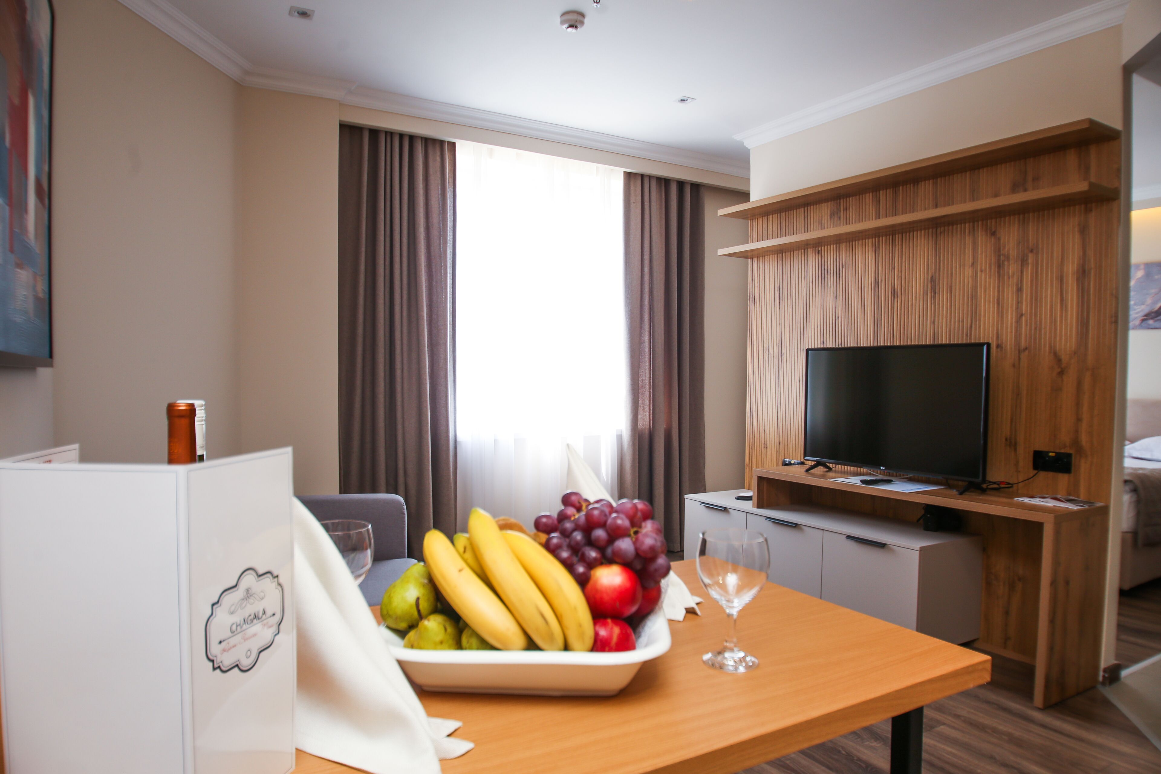 Quarto de hotel com escrivaninha de madeira, televisão, cesta de frutas e minibar.