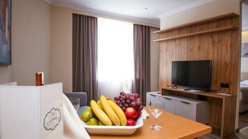 Quarto de hotel com escrivaninha de madeira, televisão, cesta de frutas e minibar.