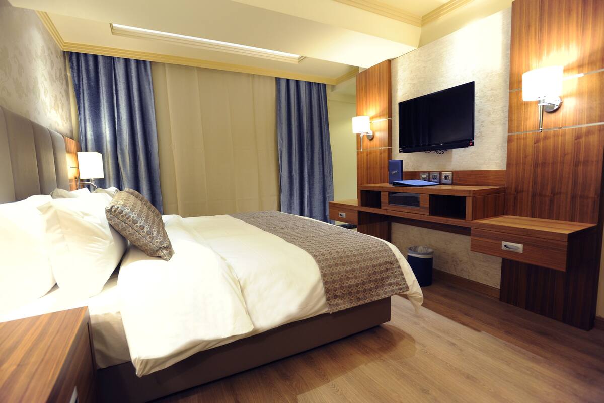 Quarto de hotel com uma cama grande, uma televisão de tela plana na parede, uma mesa com computador e uma pequena área de estar.