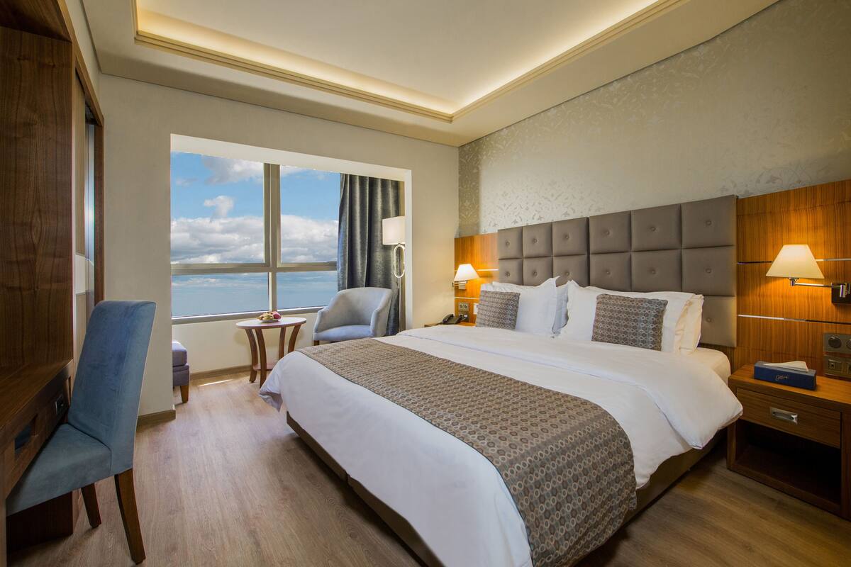 Quarto de hotel com cama grande, uma cadeira, uma mesa pequena e vista para o mar.