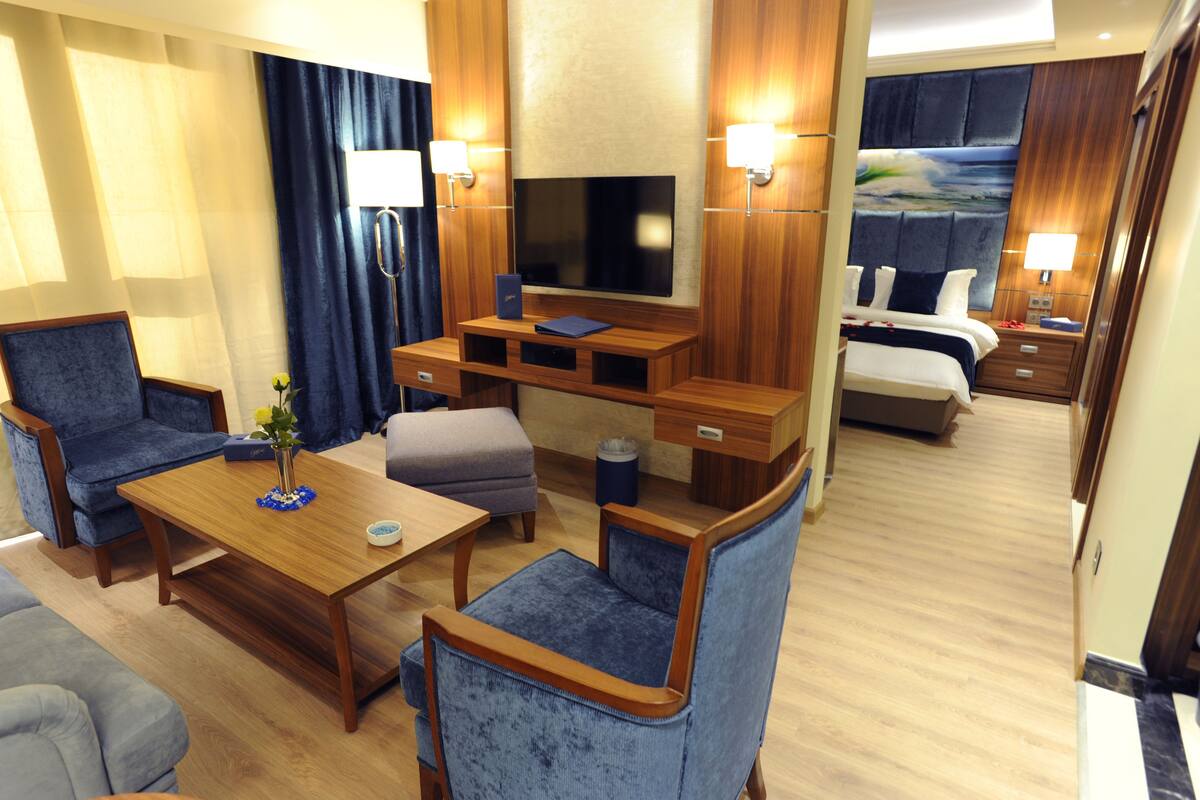 Quarto de hotel com sofá, poltrona, televisão e cama.