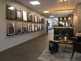 Um corredor com obras de arte emolduradas nas paredes, uma área de estar com uma mesa redonda e uma receção ao fundo.