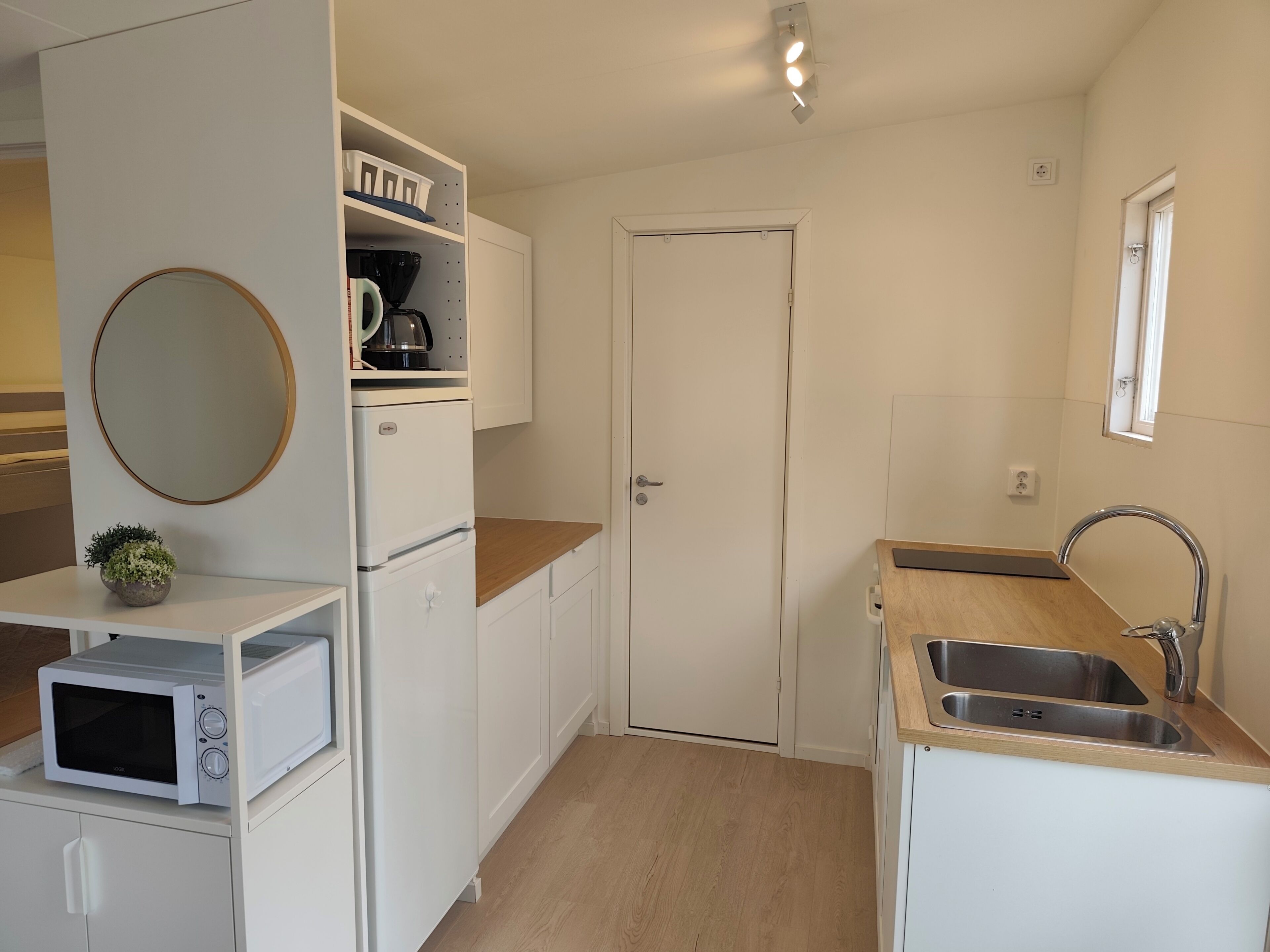 Uma cozinha compacta com armários brancos, micro-ondas, pia e uma porta que dá para outro quarto.