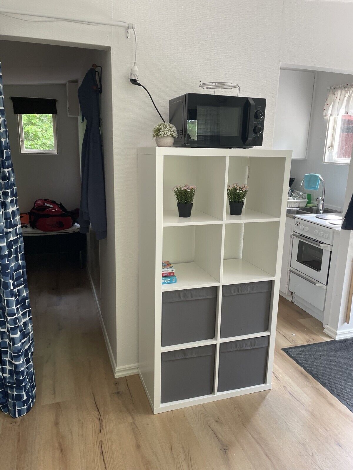 Uma cozinha compacta com micro-ondas, uma pia pequena e uma janela com cortinas.