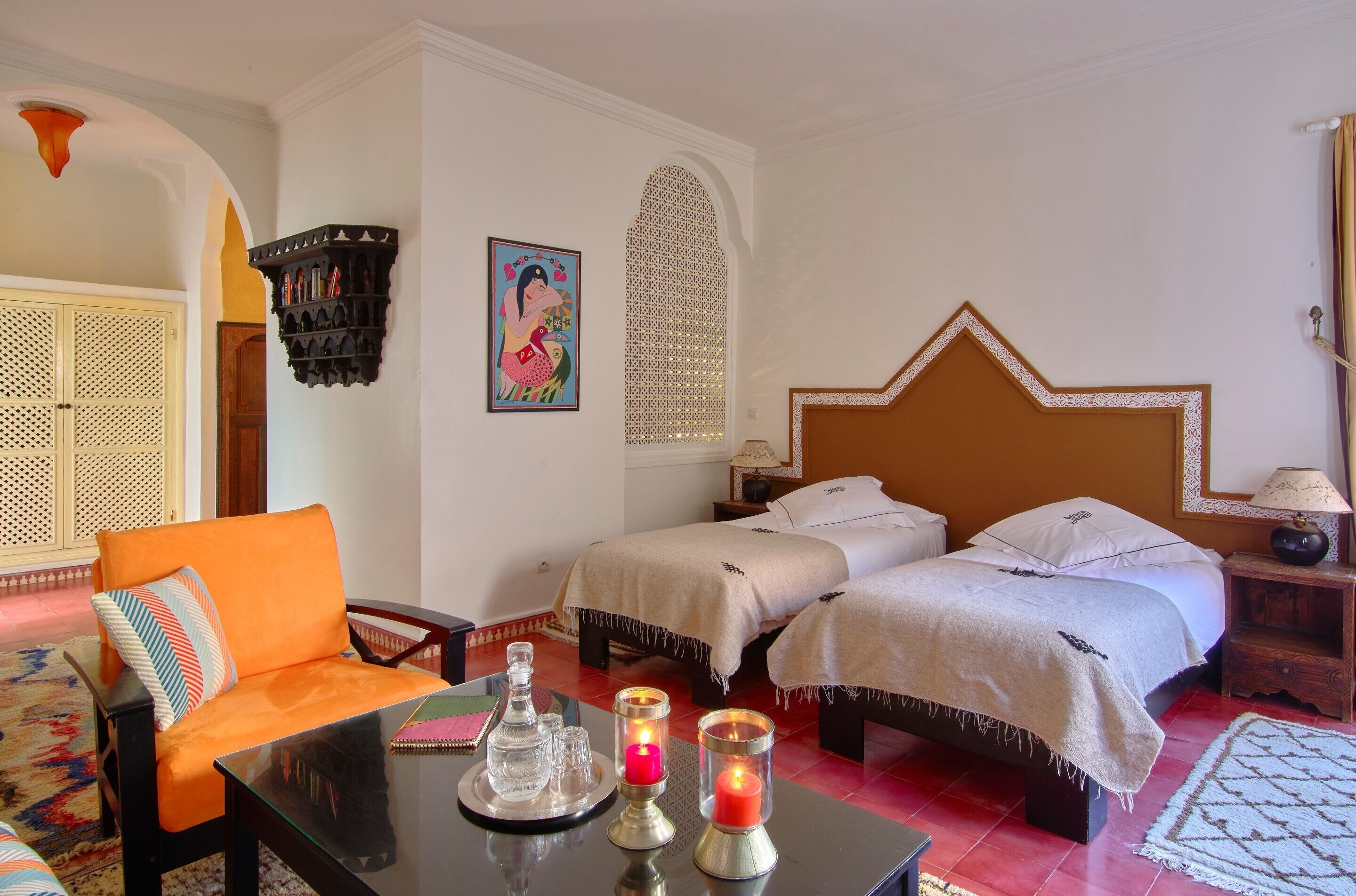 Quarto com duas camas, um sofá, uma mesa com velas e objetos decorativos.