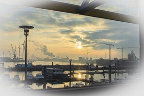 Um porto com barcos, uma grua e turbinas eólicas ao fundo.