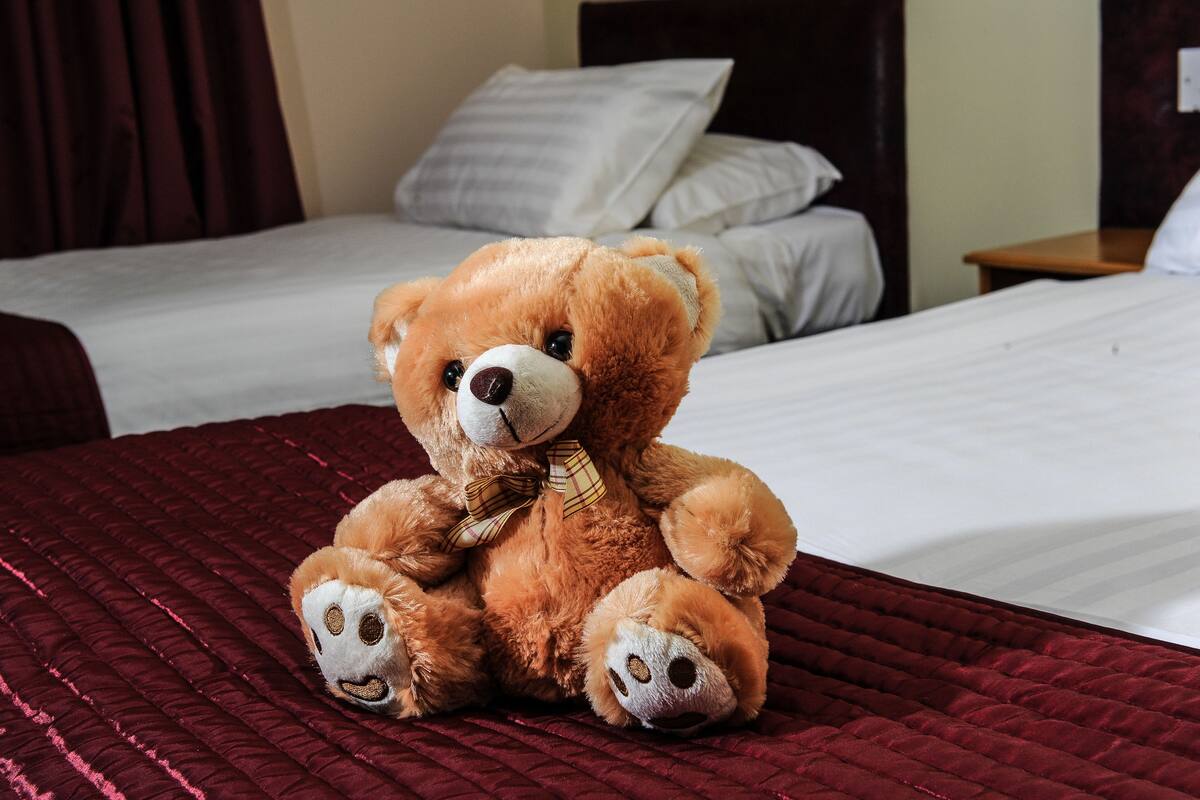Um urso de pelúcia macio sobre uma cama com cobertura acolchoada vermelha.