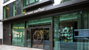 Entrada de um hotel com fachada de vidro, um logotipo circular e uma placa com a inscrição "LE SAINT ANTOINE".