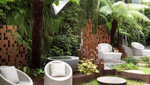Um jardim exuberante com áreas de estar, um espelho d'água e diversas plantas.