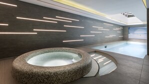 Piscina interior moderna com hidromassagem em mosaico, iluminação embutida e claraboia.
