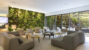 Uma sala de estar moderna com uma grande parede verde, assentos confortáveis, uma TV de tela plana e vista para o exterior.