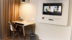 Quarto moderno com uma escrivaninha de madeira, uma cadeira, televisão fixada na parede e um cesto de lixo.