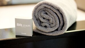 Uma toalha enrolada com etiqueta que diz 'ibis Styles hotels sabonete' sobre uma superfície preta.