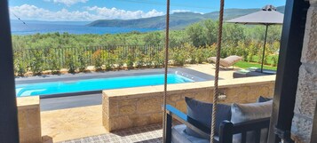 Uma piscina com vista para o mar, uma parede de pedra e uma cadeira de balanço.