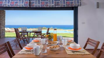 Mesa de jantar posta com itens de café da manhã, vista para o oceano e uma parede de pedra.
