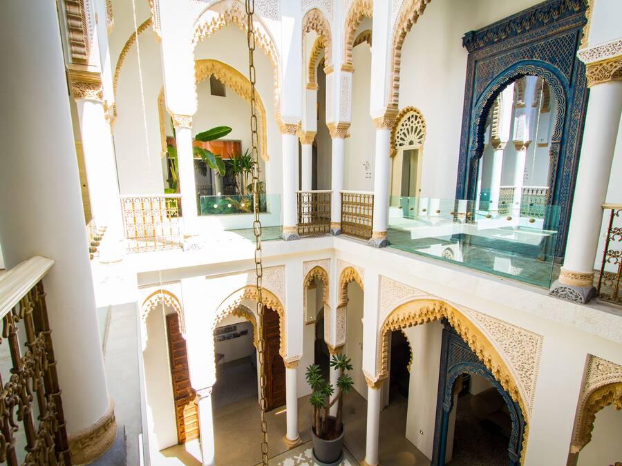 Um átrio de vários níveis com arcos ornamentados e guarda-corpo de vidro, com vista para um pátio.