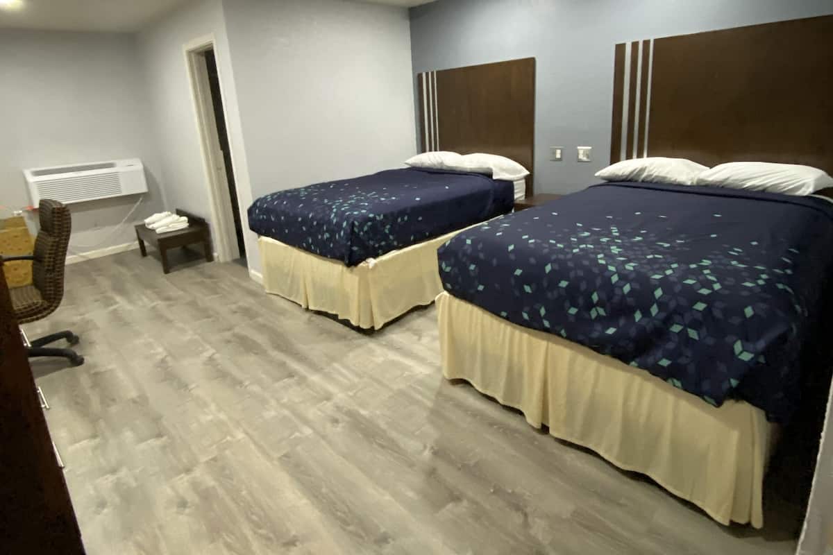 Quarto de hotel com duas camas, uma mesinha, aparelho de ar condicionado e chão de madeira.