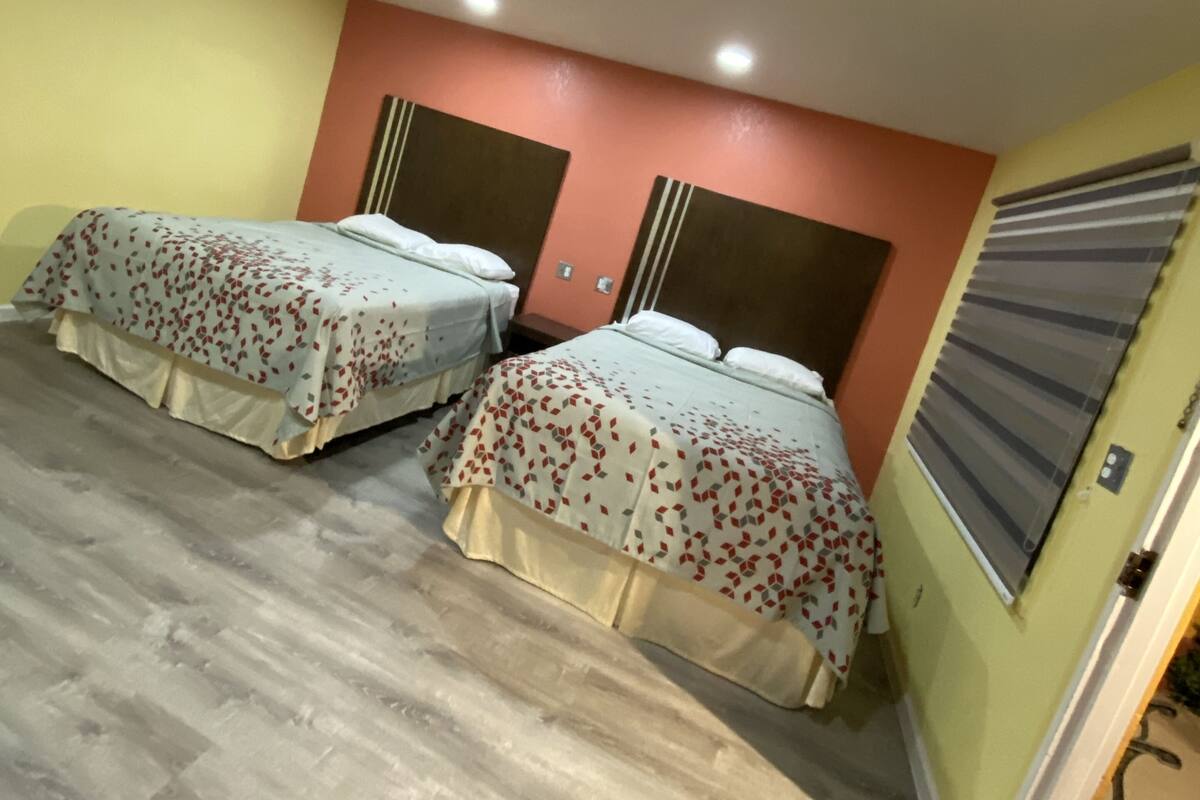 Quarto com duas camas, soalho de madeira e persiana riscada.