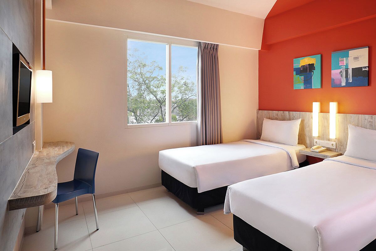 Quarto de hotel com duas camas, uma escrivaninha, uma cadeira, televisão e obras de arte na parede.