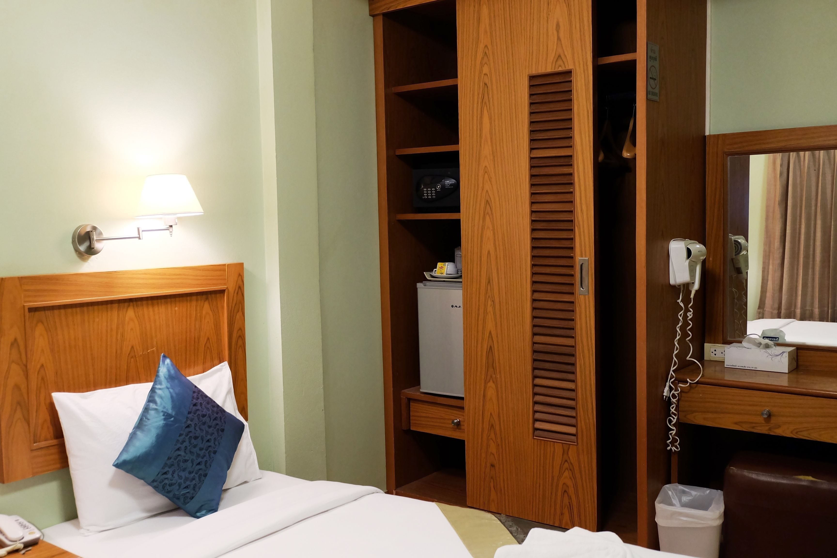 Quarto de hotel com cama, mesa de cabeceira, luminária, guarda-roupa, espelho, lixeira e telefone.