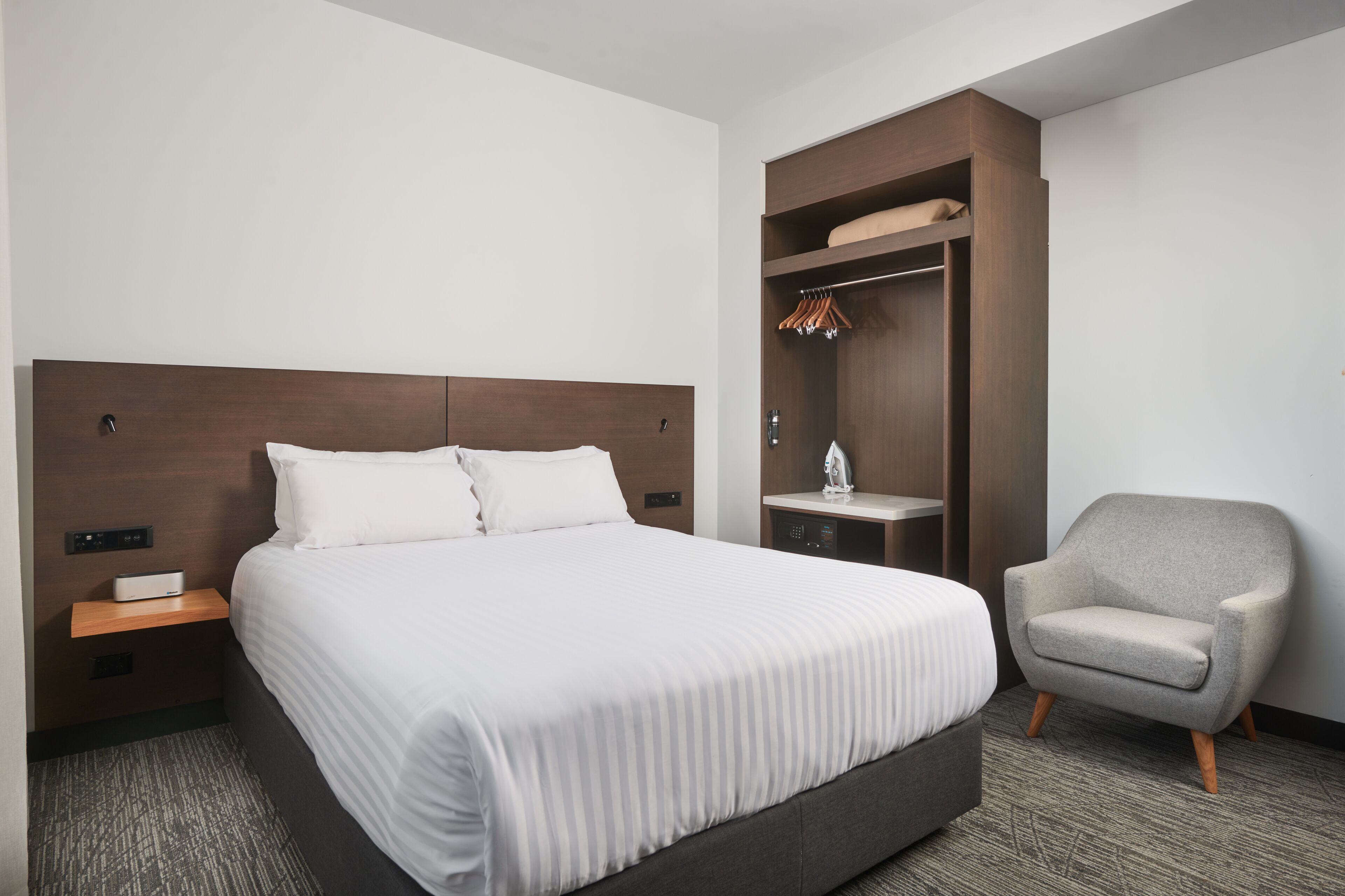 Quarto de hotel com cama grande, mesa de cabeceira, guarda-roupa e uma cadeira.