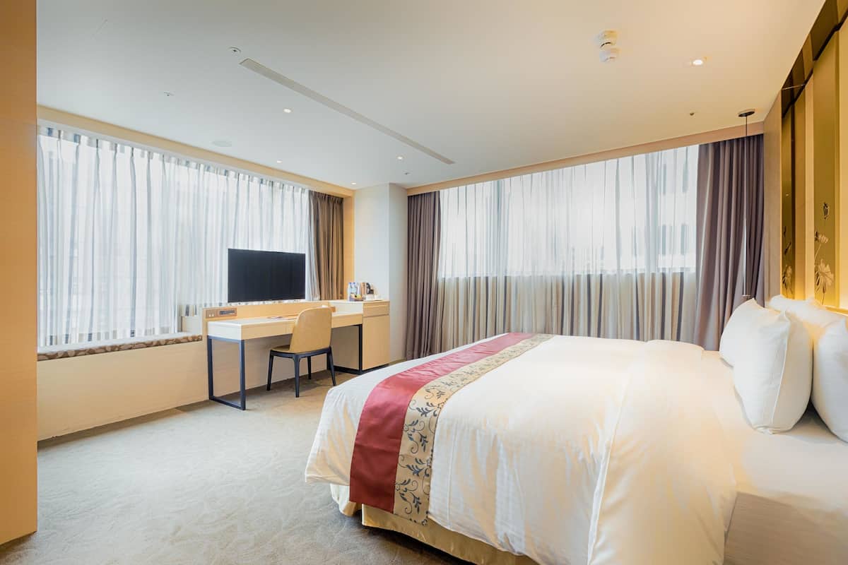 Quarto de hotel com uma cama grande, uma mesa e uma televisão.