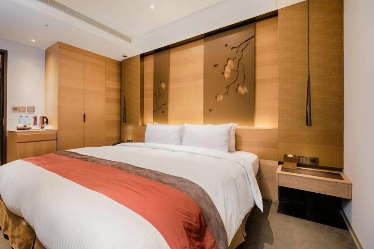 Quarto de hotel com uma cama grande, guarda-roupa de madeira, mesa de cabeceira e luminária na parede.