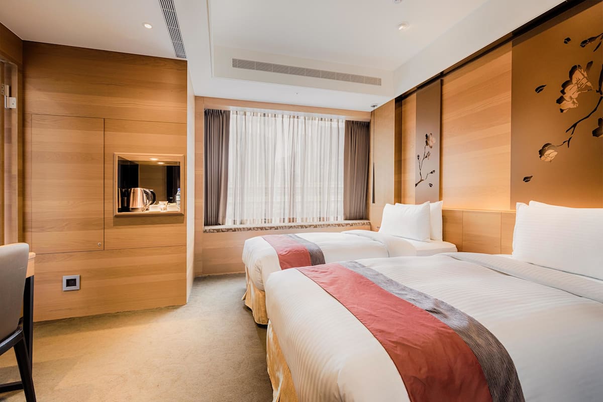 Quarto de hotel com duas camas, parede revestida em madeira, janela com cortinas, máquina de café e uma obra de arte pendurada na parede.
