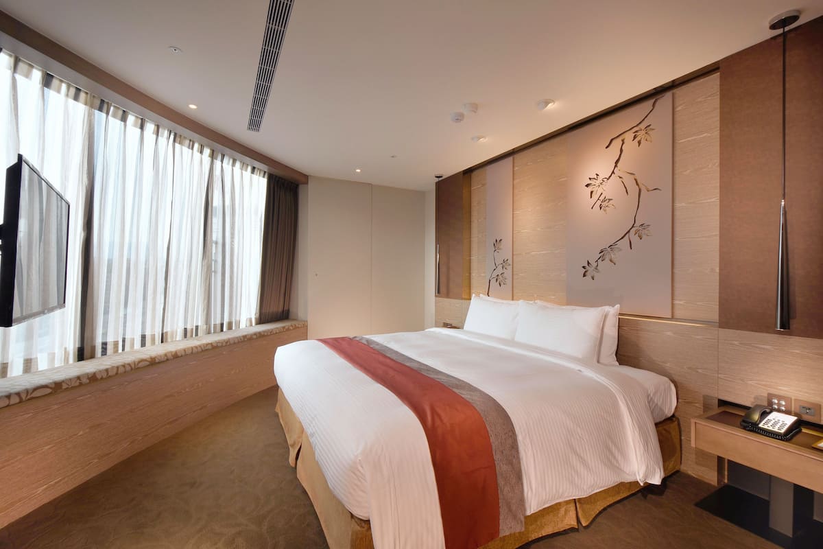 Quarto de hotel com uma cama grande, mesa de cabeceira com telefone e janela com cortinas.