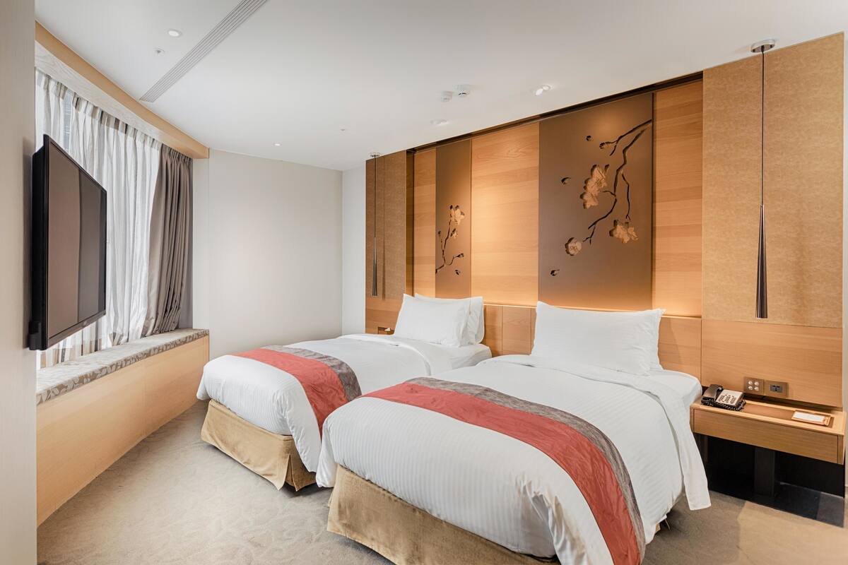 Quarto de hotel moderno com duas camas, televisão de tela plana fixada na parede e uma parede de madeira com design de galho decorativo.