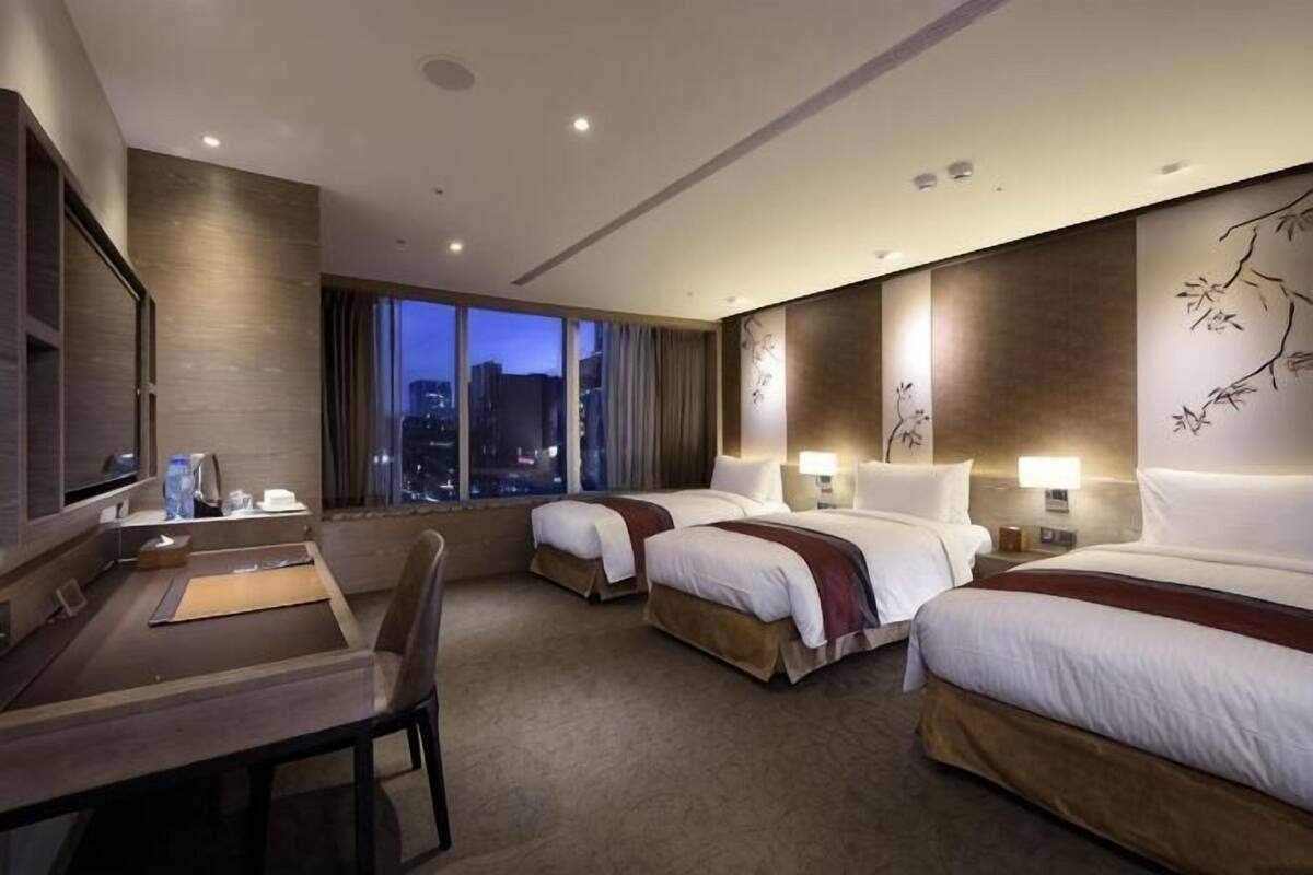 Quarto de hotel com escrivaninha, duas camas, televisão e vista para a cidade.