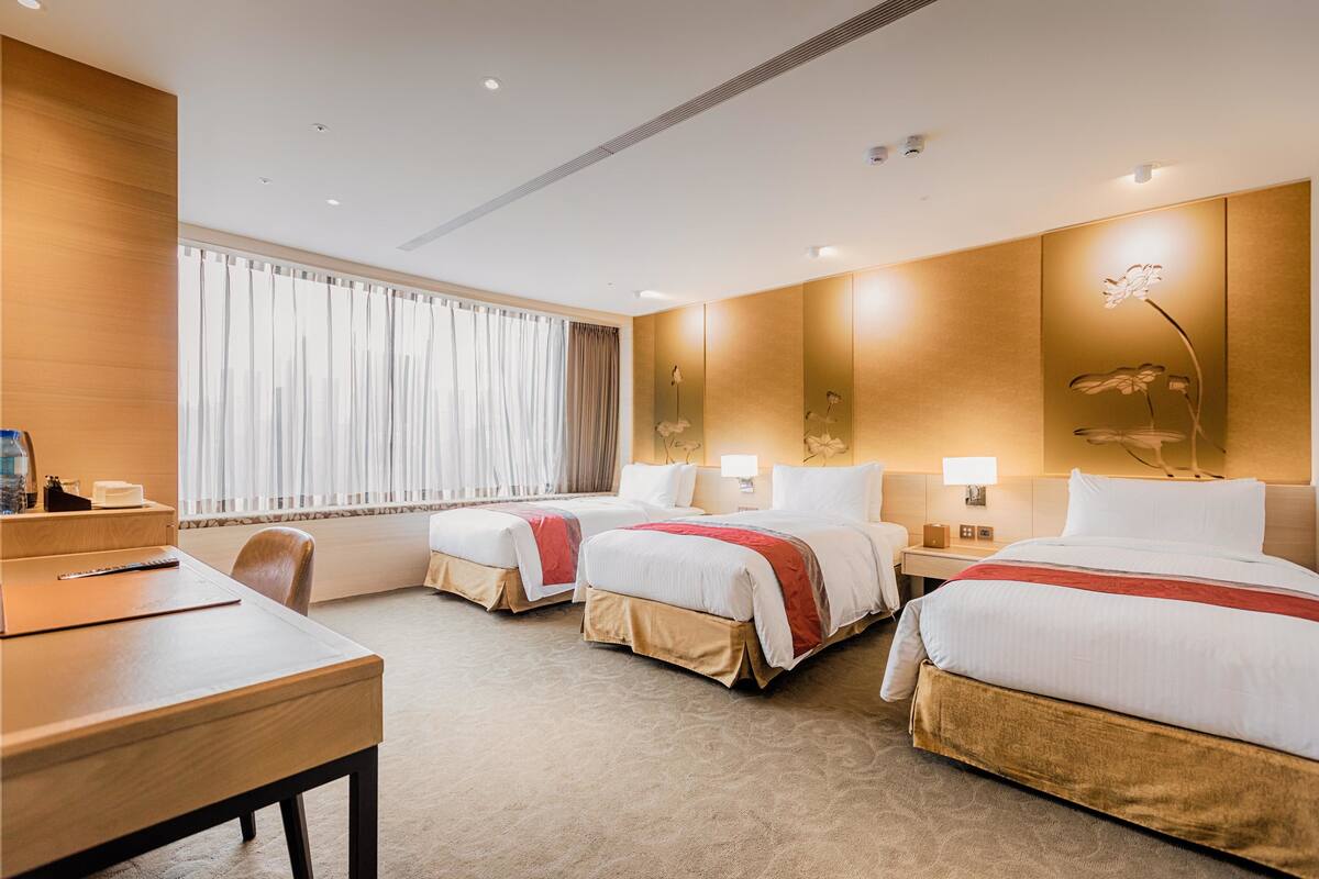 Quarto de hotel com duas camas, uma escrivaninha e uma janela grande com cortinas.