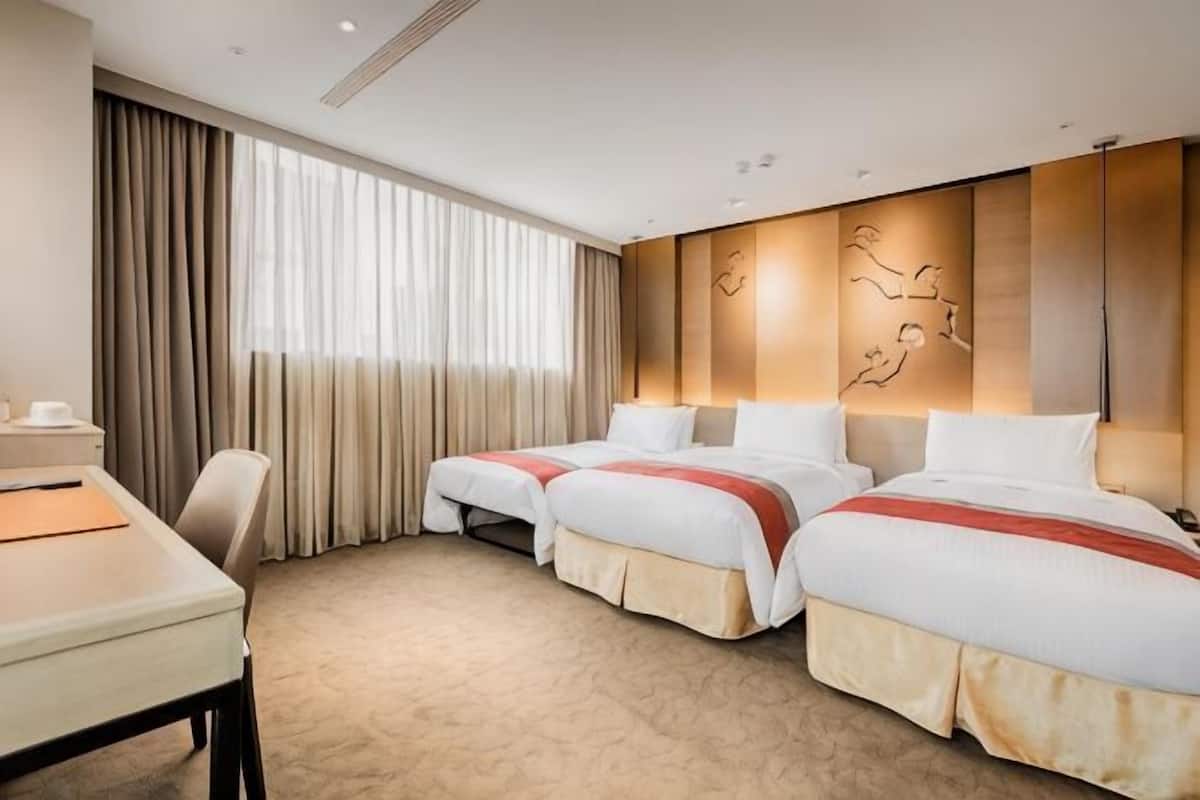 Quarto de hotel com duas camas, uma escrivaninha e uma janela grande com cortinas.