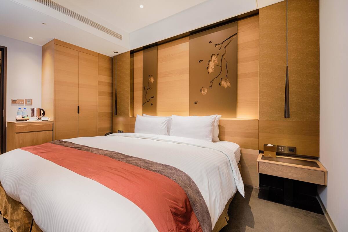 Quarto de hotel moderno com uma cama grande, guarda-roupa de madeira e mesa de cabeceira com abajur.