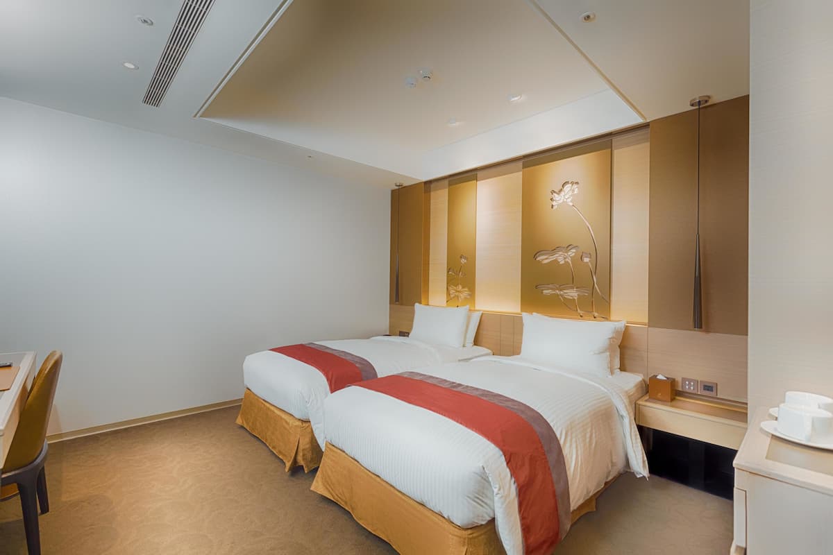 Quarto de hotel com duas camas, uma escrivaninha e uma cadeira.