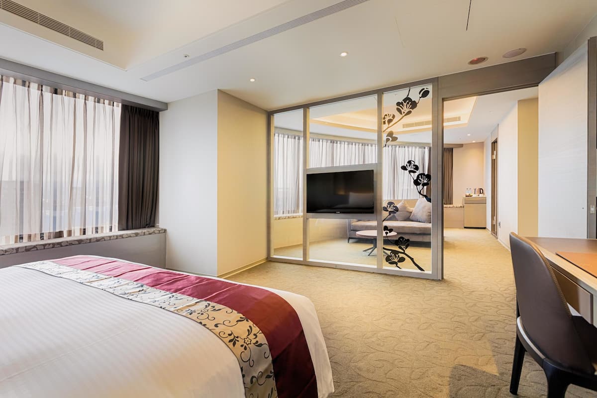 Quarto de hotel com cama, escrivaninha, televisão e porta de correr para uma varanda.