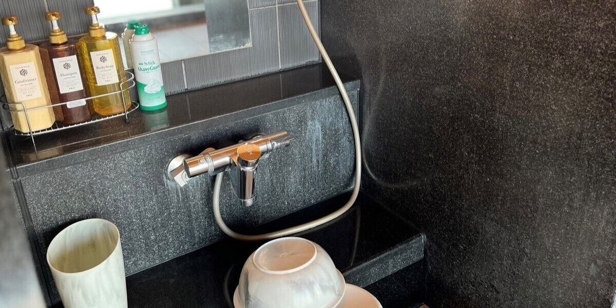 Casa de banho com bancada preta, chuveiro e artigos de higiene num armário.